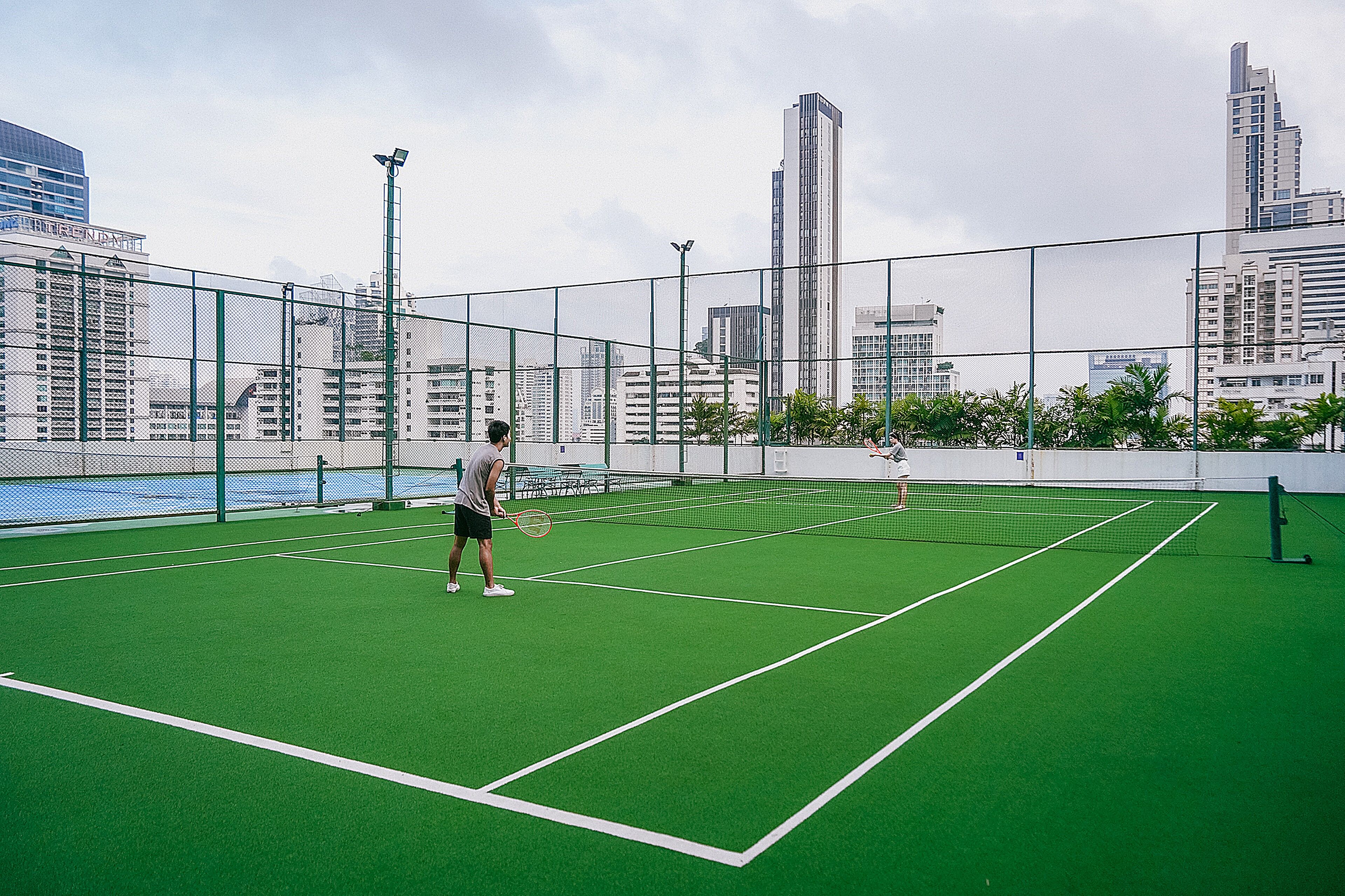 Uma quadra de tênis ao ar livre com um horizonte urbano ao fundo.