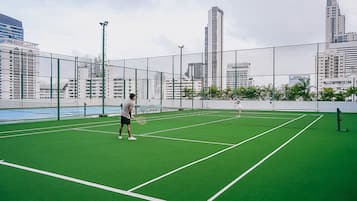 Uma quadra de tênis ao ar livre com um horizonte urbano ao fundo.