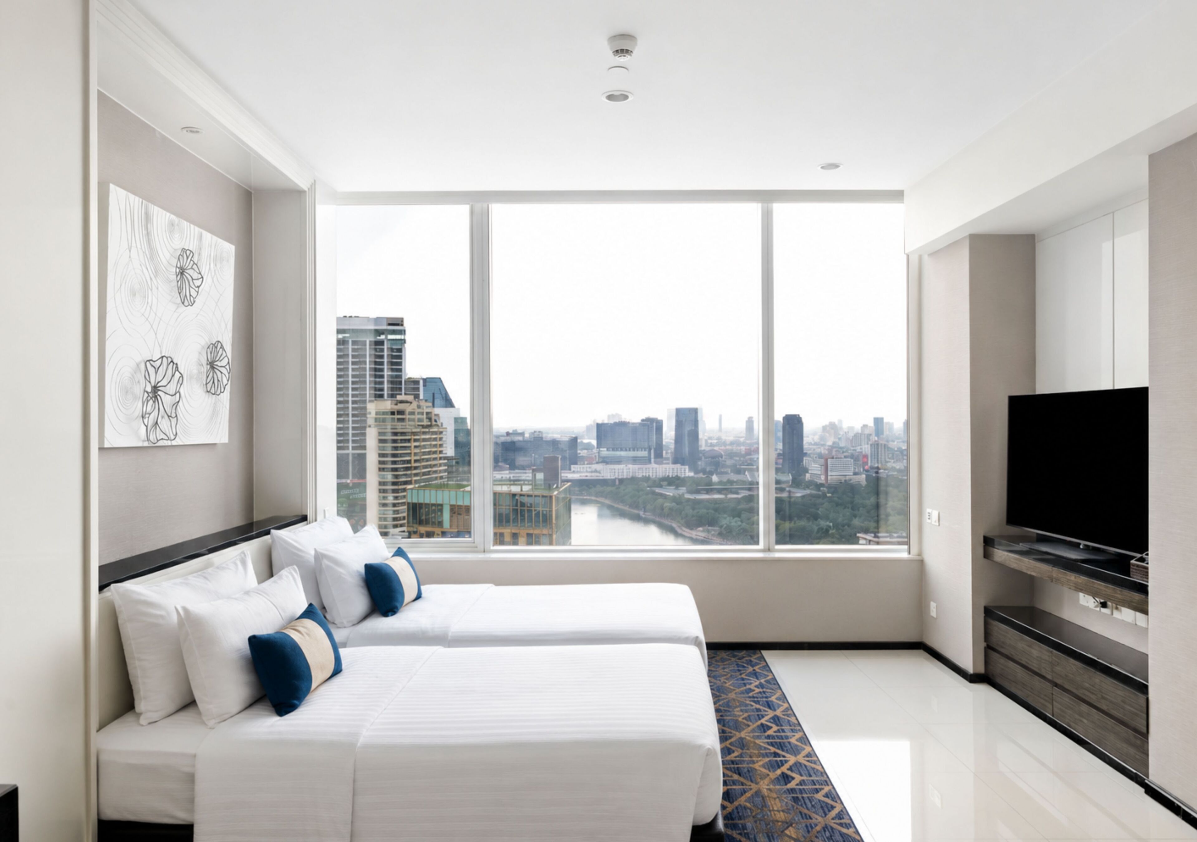 Quarto de hotel com duas camas, uma janela grande com vista para a cidade e uma televisão de tela plana.