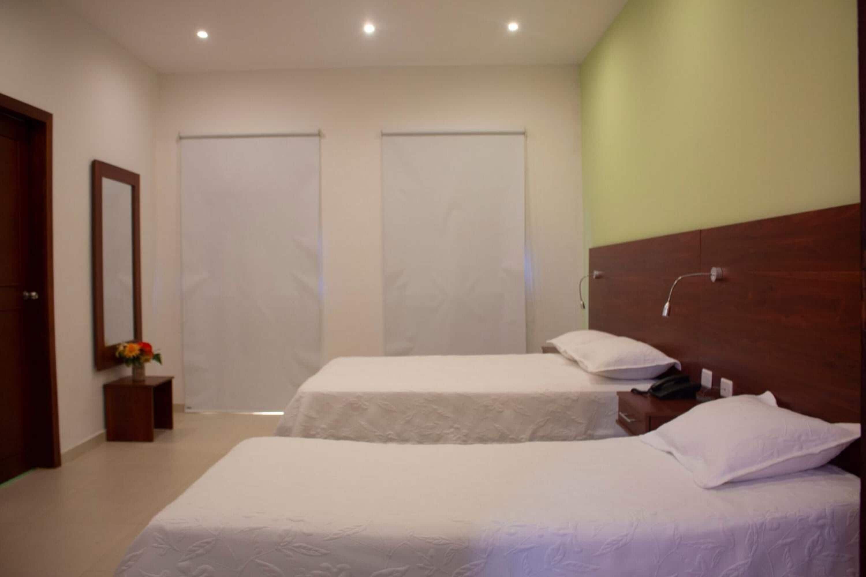 Quarto de hotel com duas camas, cabeceira de madeira, mesa de cabeceira com telefone e uma pequena mesa com um vaso de flores.