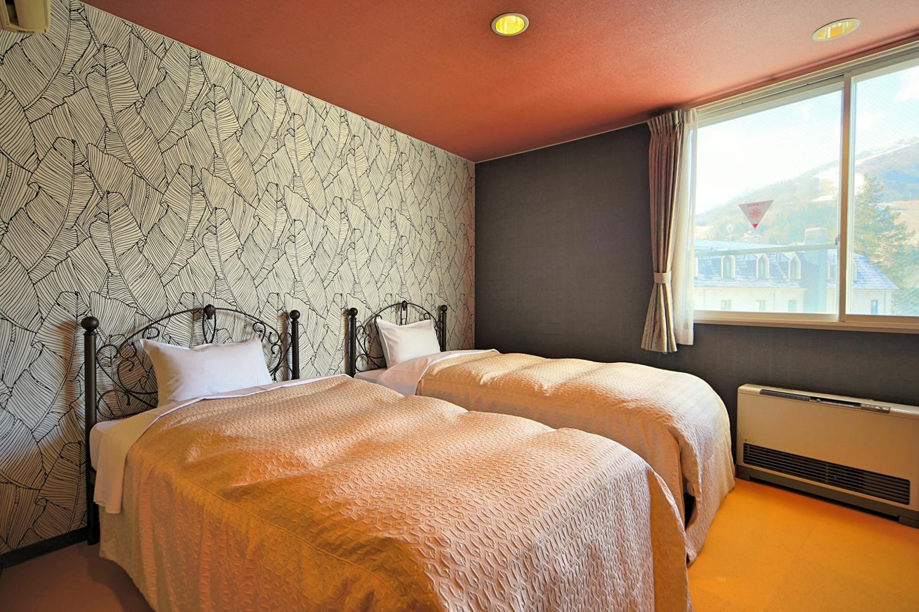Quarto com duas camas, papel de parede estampado, radiador e janela com cortinas.