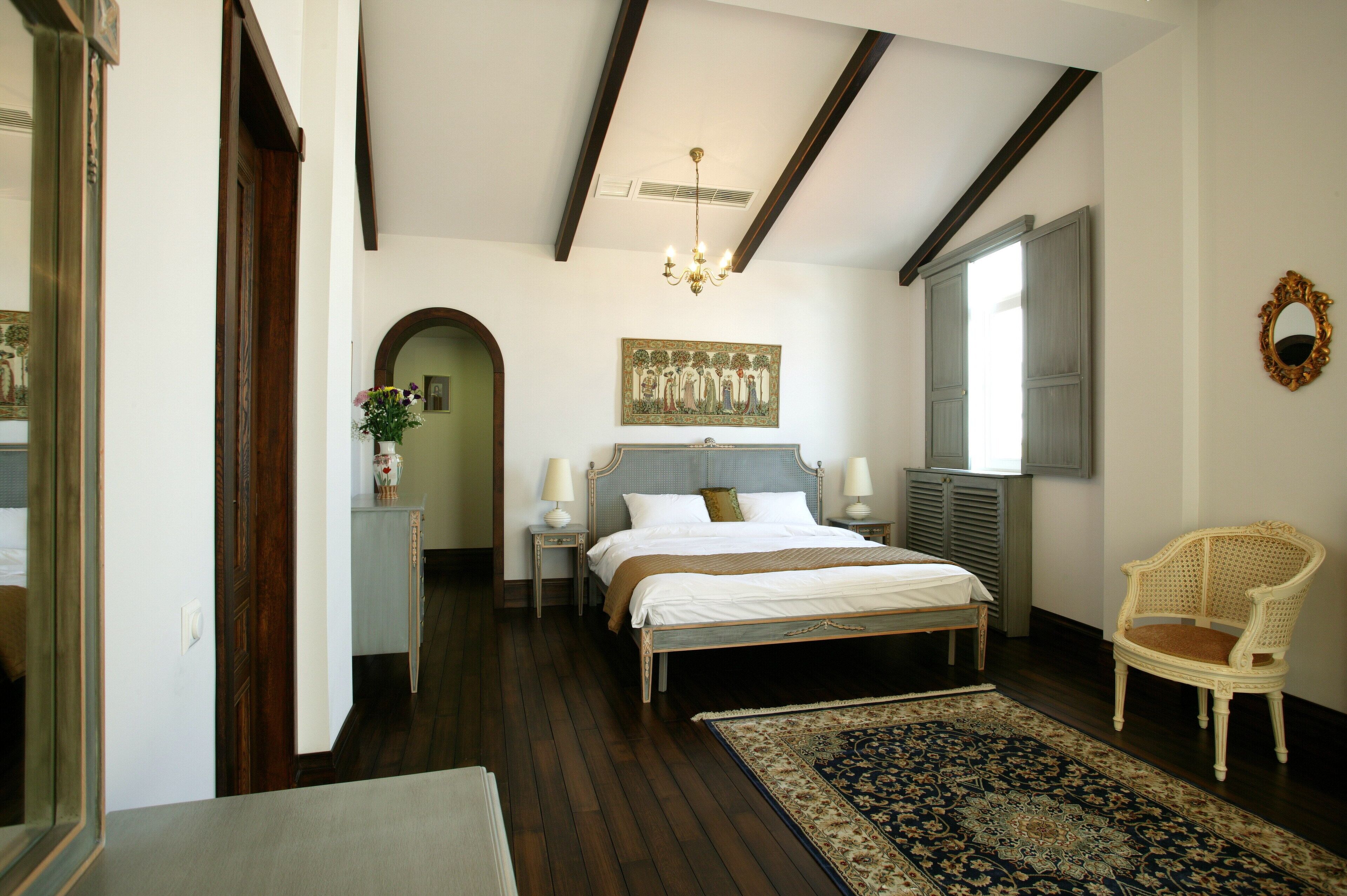 Quarto com cama grande, mesa de cabeceira, cadeira, lustre e um quadro na parede.