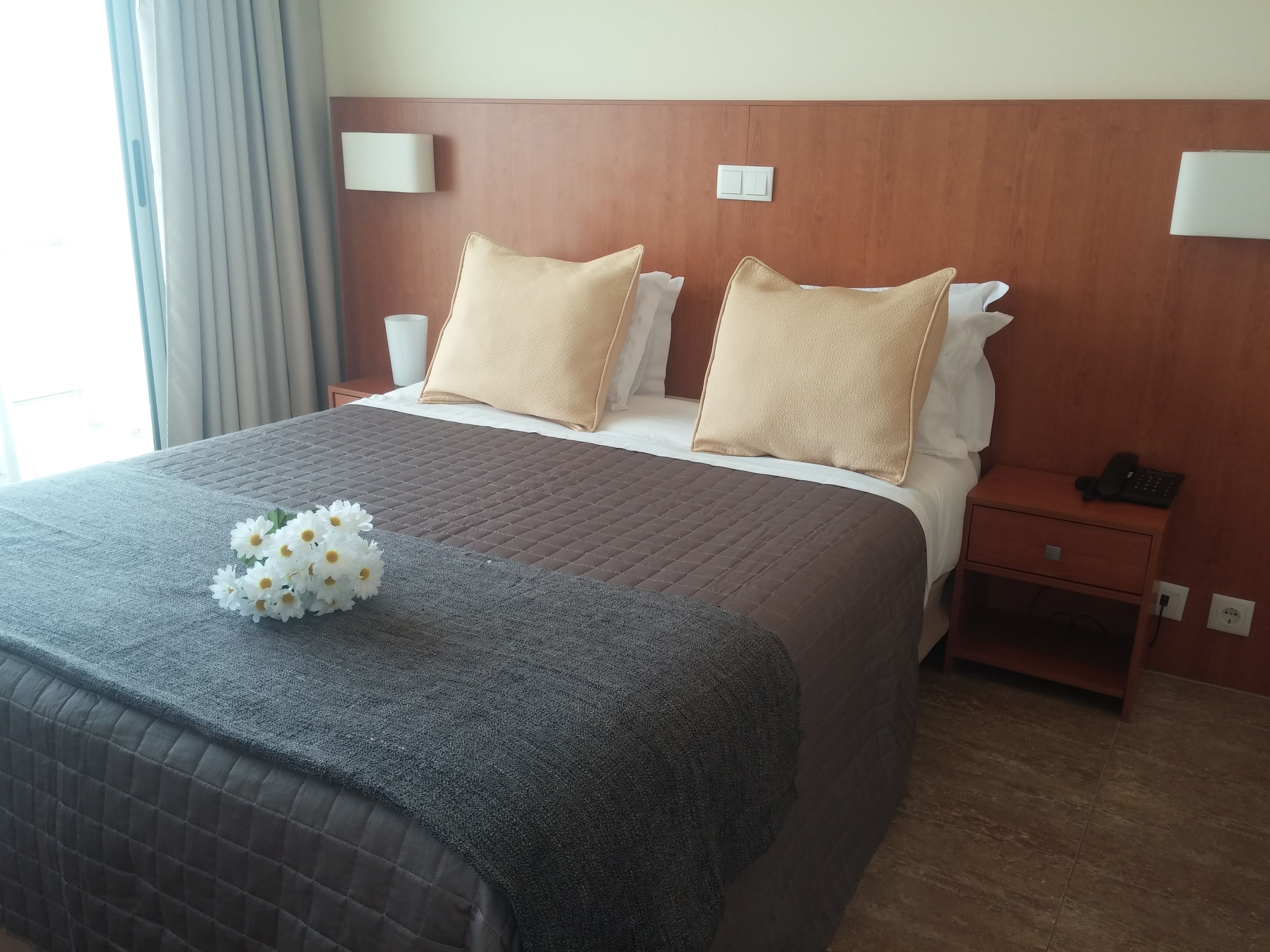Quarto de hotel com uma cama grande, duas mesas de cabeceira e uma luminária fixada na parede.