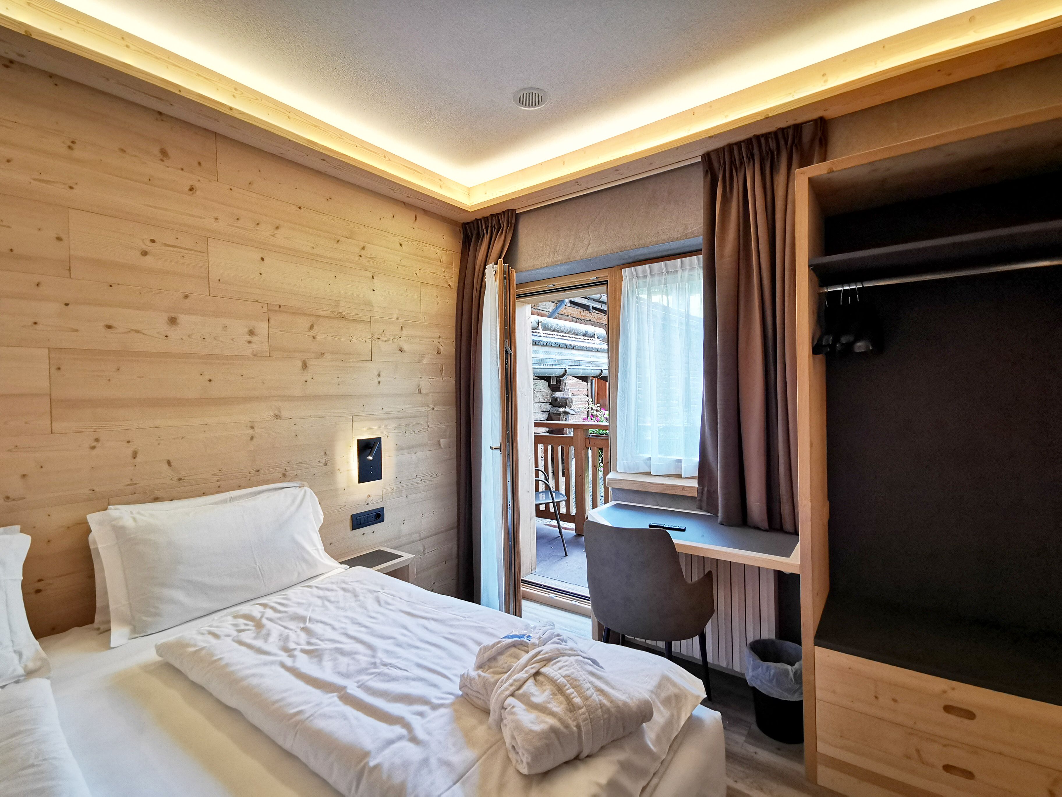 Quarto com painéis de madeira, uma cama, uma escrivaninha e uma cadeira.
