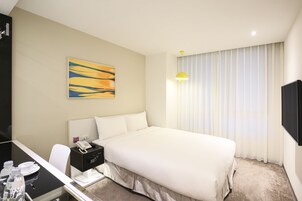Quarto de hotel com cama, mesa de cabeceira, luminária, obra de arte e televisão.