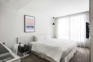 Quarto de hotel com uma cama, uma mesa com telefone, um quadro na parede e uma janela com cortinas.