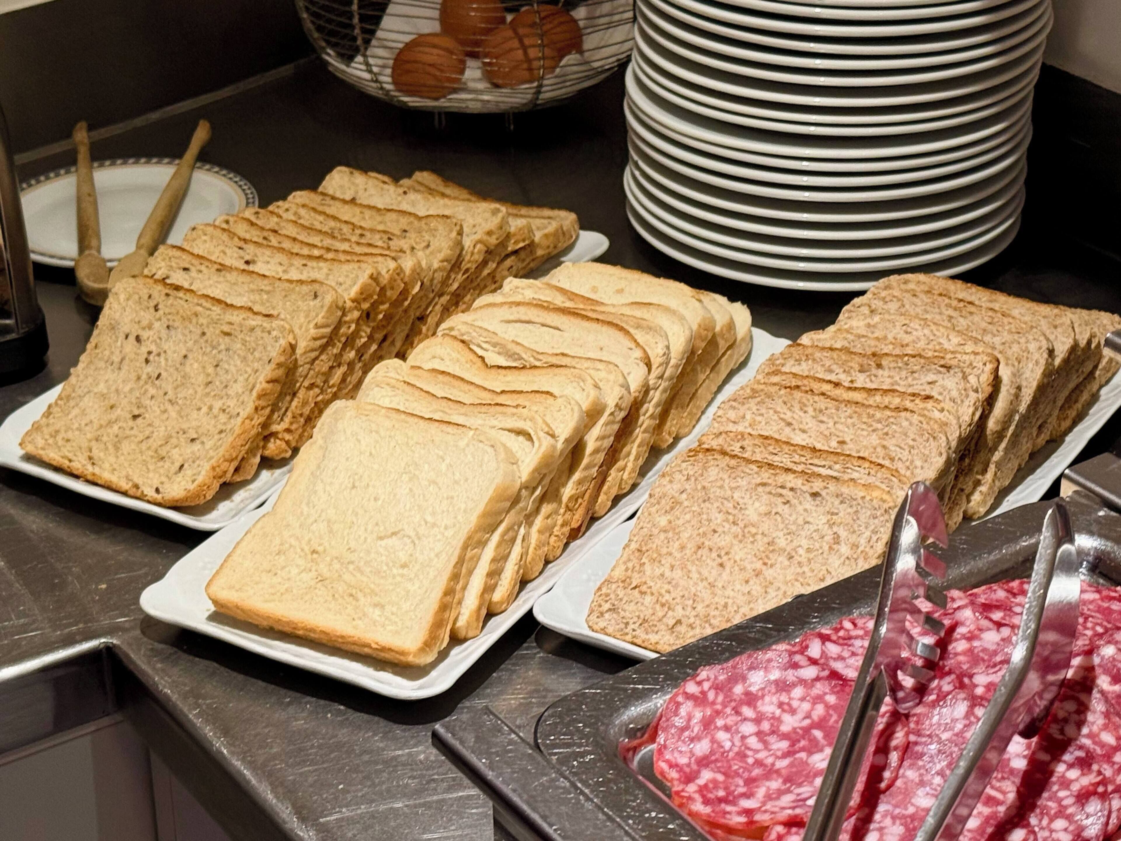 Uma mesa de buffet com pão fatiado e um tabuleiro de salame fatiado.