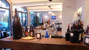Uma área de bar com diversos frascos e copos, uma garrafa de vinho grande e uma televisão ao fundo.