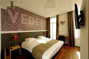 Quarto de hotel com uma cama grande, uma escrivaninha, uma TV e uma parede decorada com fotografias.