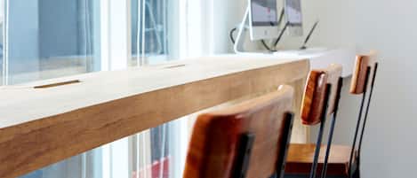 Uma mesa de madeira com um laptop e dois monitores em um suporte, posicionada perto de uma janela com persianas.