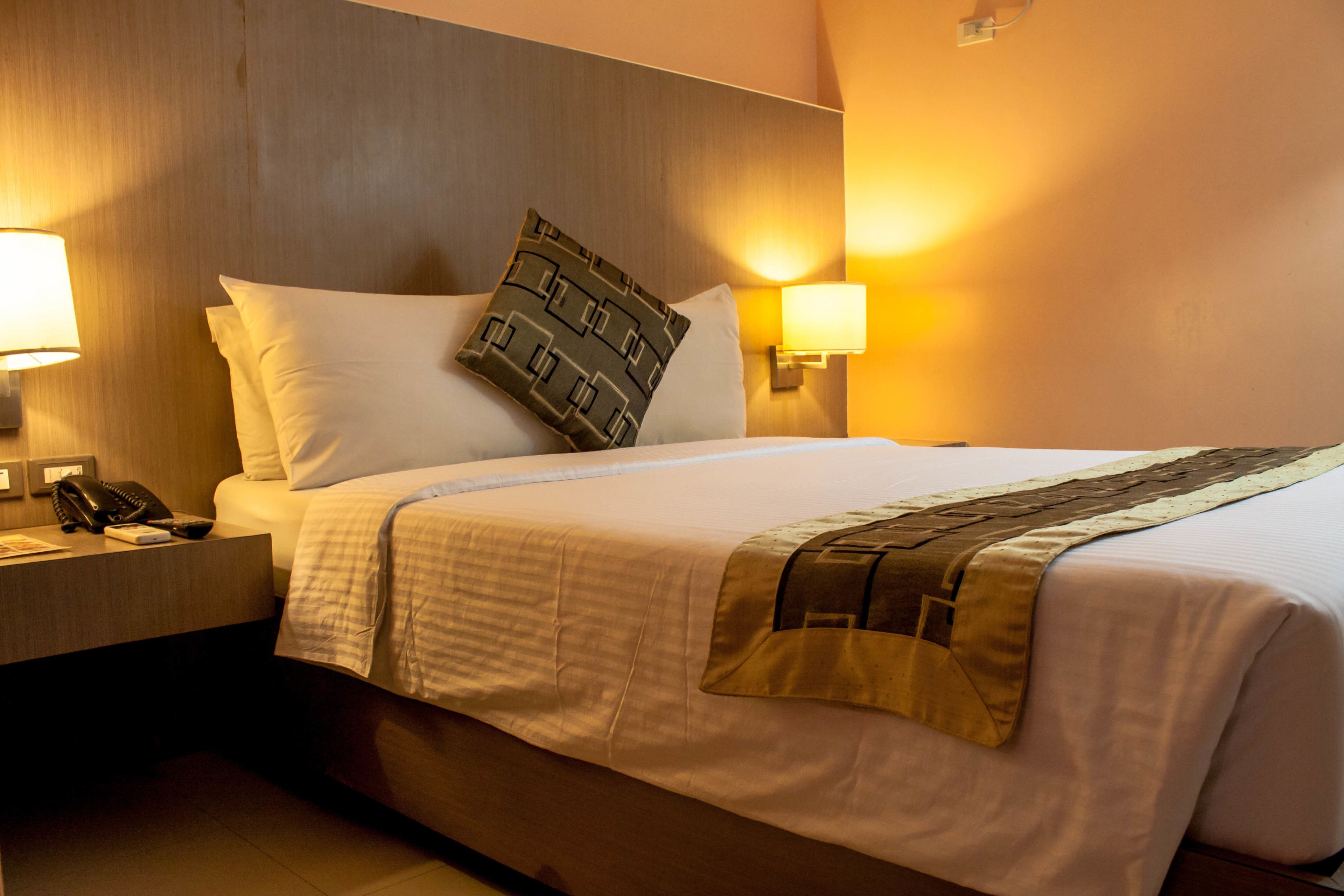 Quarto de hotel com cama bem arrumada, mesa de cabeceira com abajur e telefone.