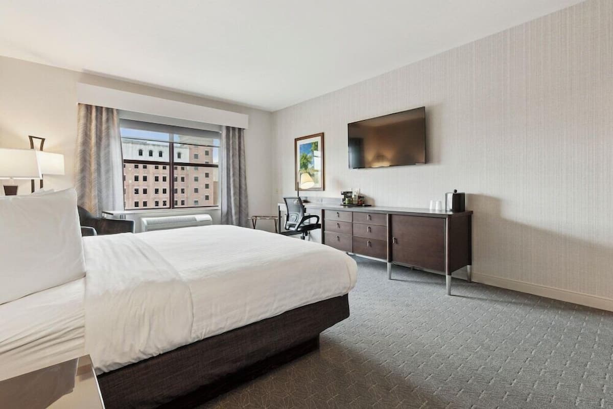 Quarto de hotel com cama, escrivaninha, cadeira, televisão e janela com vista para a cidade.