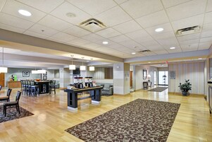 Um hall amplo com piso de madeira, estação de café central, áreas de estar e tapete estampado.