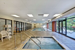 Uma área de piscina interna com paredes de vidro transparente, piscina com hidromassagem e vista para o exterior.