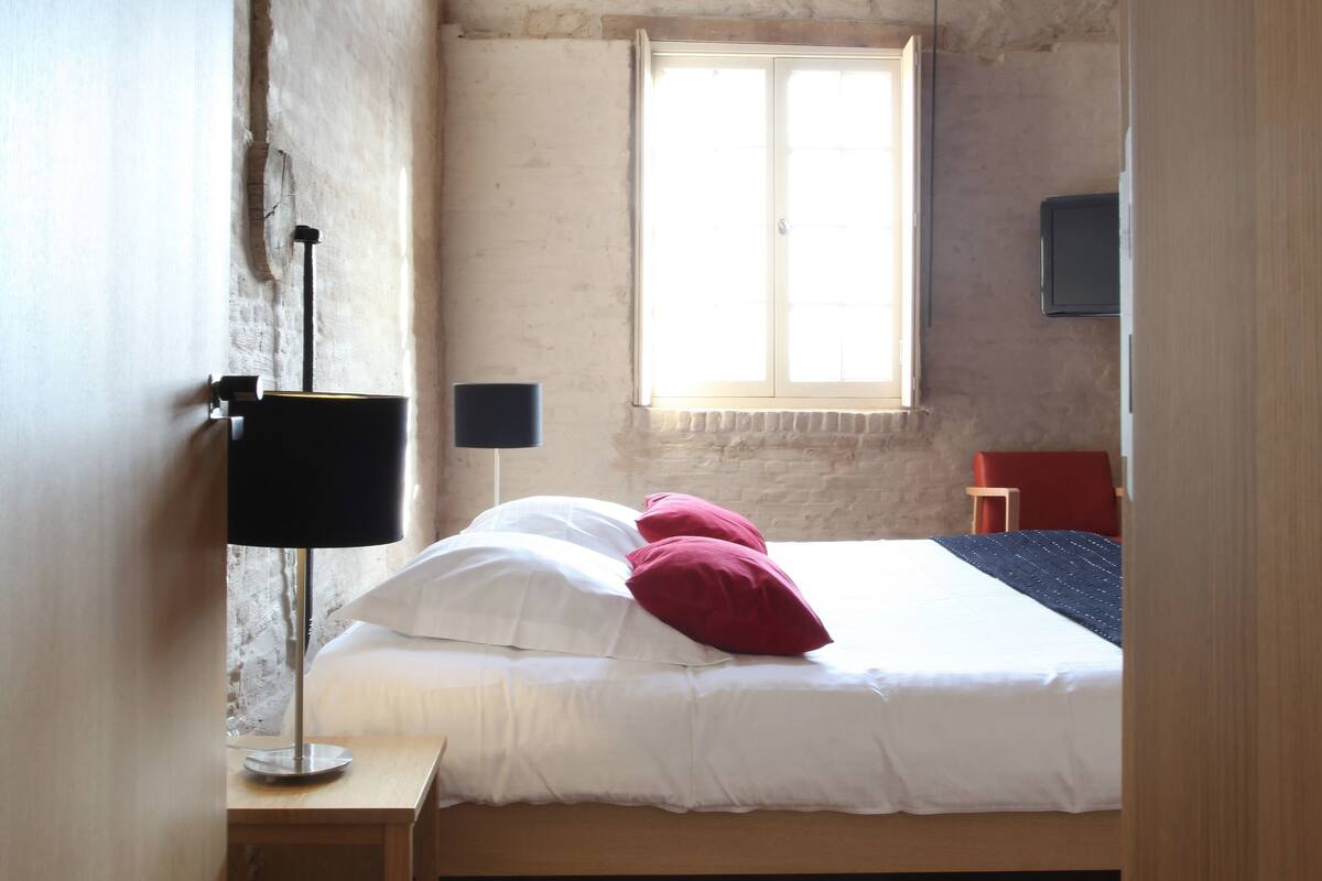 Quarto com cama, janela, escrivaninha e cadeira.