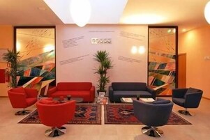 Um hall moderno com sofás vermelhos e pretos, uma mesa de centro e um vaso de planta.