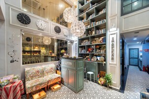 Uma área de recepção com balcão verde, sofá estampado e estante repleta de livros.