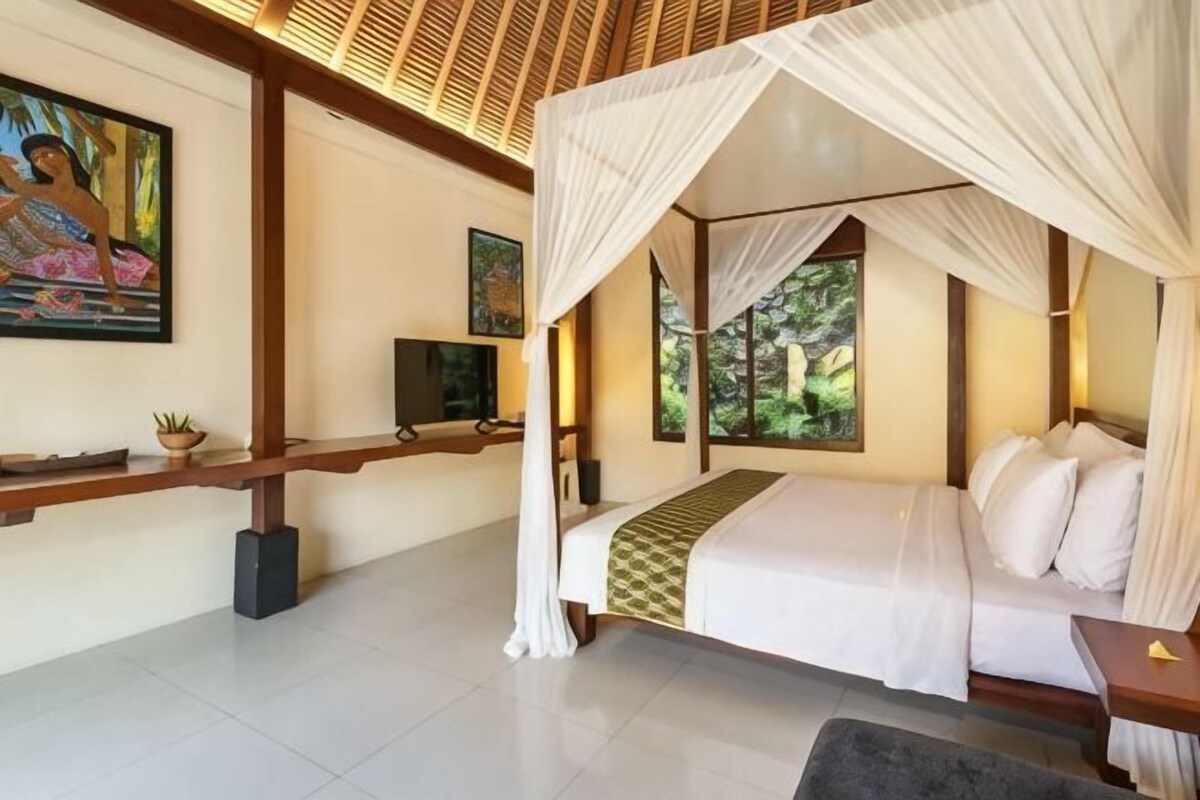 Quarto com cama, televisão, escrivaninha e janela com vista para área verde.
