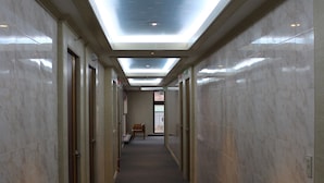 Corredor longo e estreito de hotel, com teto skylight, paredes de mármore e portas de acesso aos quartos.