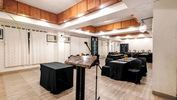 Uma sala de conferências com mesas, cadeiras, um pódio e um lustre.