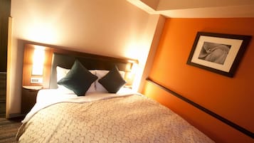 Quarto de hotel com cama, mesa de cabeceira, quadro na parede e uma parede de destaque na cor laranja.