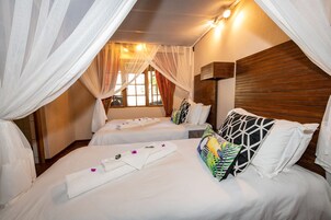 Quarto de hotel com duas camas, roupa de cama branca, cabeceira de madeira e uma janela com cortinas.