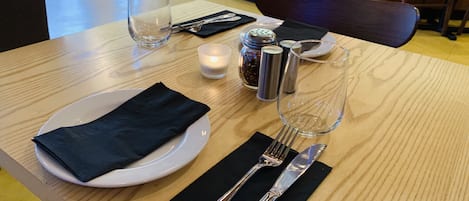 Uma mesa de jantar posta com prato, talheres, copo, vela e saleiro e pimenteiro.