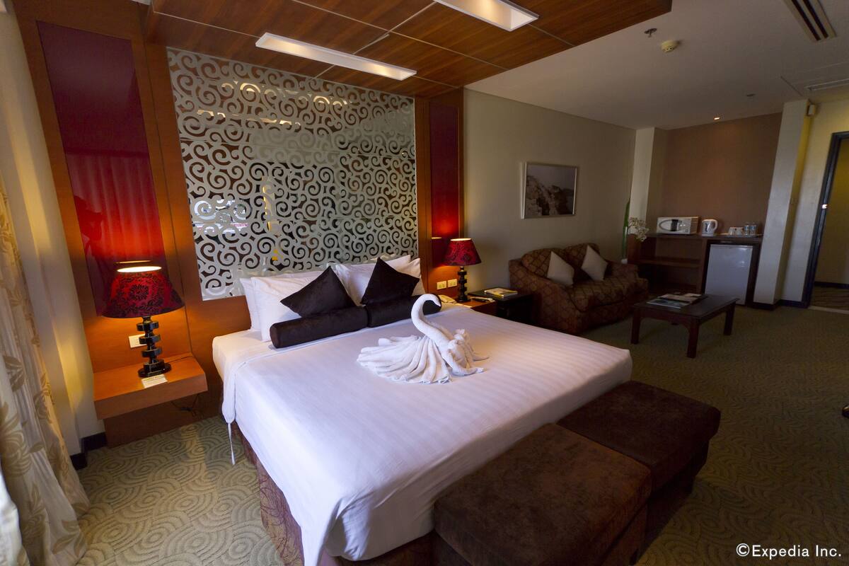 Quarto de hotel com cama grande, sofá, mesa pequena e micro-ondas.