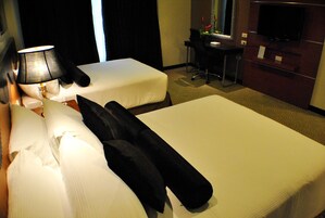 Quarto de hotel com duas camas, uma escrivaninha, uma cadeira, uma televisão e um abajur.