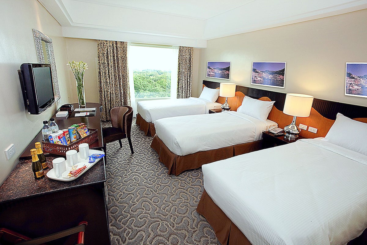 Quarto de hotel com duas camas, uma escrivaninha com televisão e vista para o exterior.