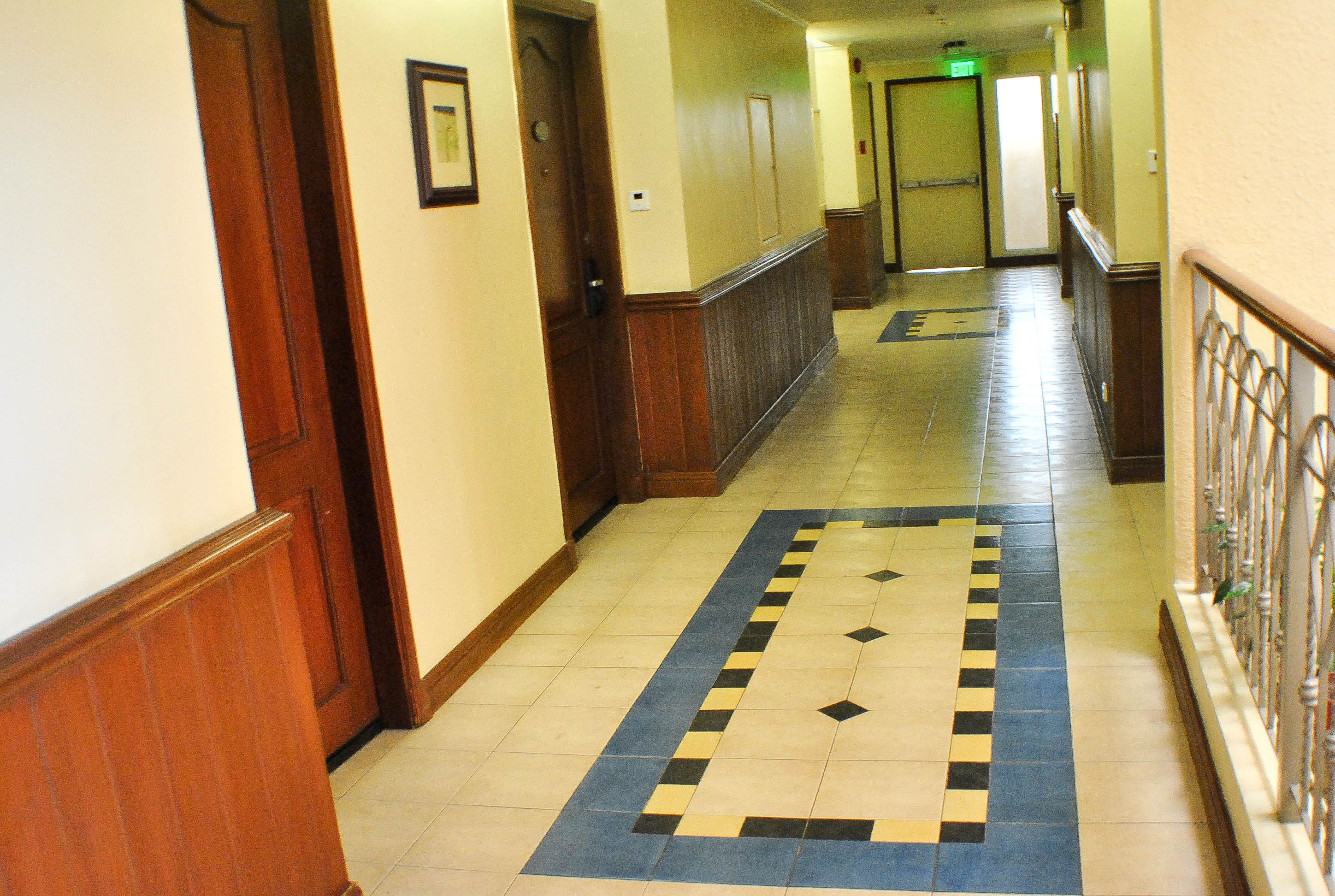 Corredor de hotel com painéis de madeira, carpete estampado e corrimão de metal à direita.