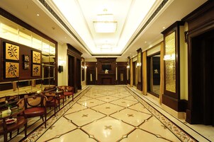 Um saguão de hotel com um corredor extenso, decoração de parede elaborada e um candelabro.