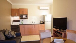 Um espaço compacto com cozinha compacta, televisão de tela plana, sofá e mesa de jantar.