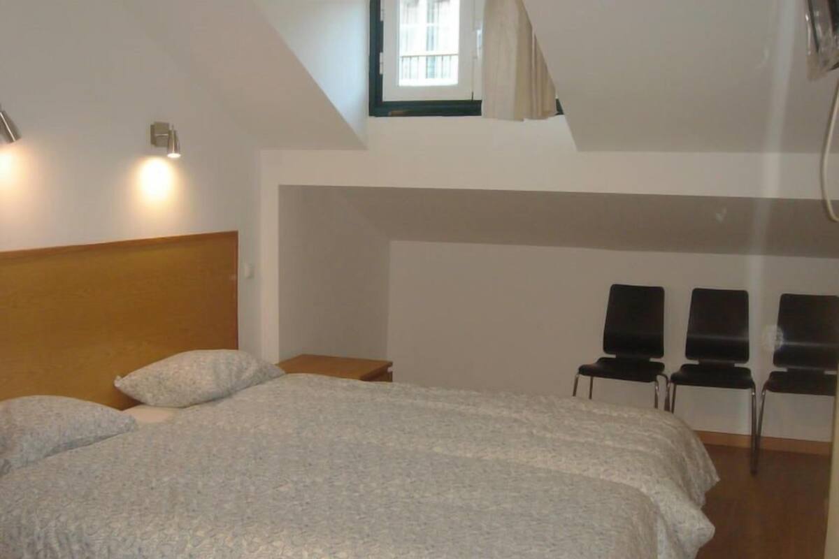 Quarto com uma cama, uma mesa de cabeceira e três cadeiras.