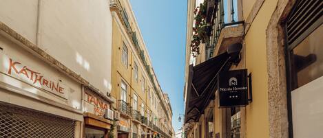 Rua estreita com lojas e um hotel chamado 'Nicola Rossio'.