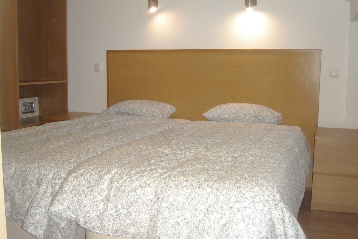 Uma cama de casal com roupa de cama floral, uma cabeceira de madeira e duas luzes fixadas na parede.