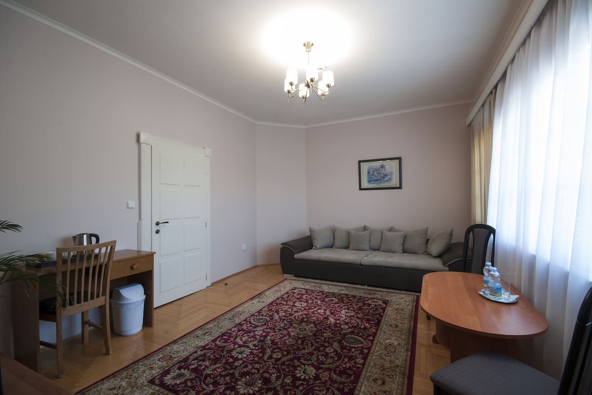 Uma sala de estar com sofá, mesa de madeira, lustre, porta e janela com cortinas.