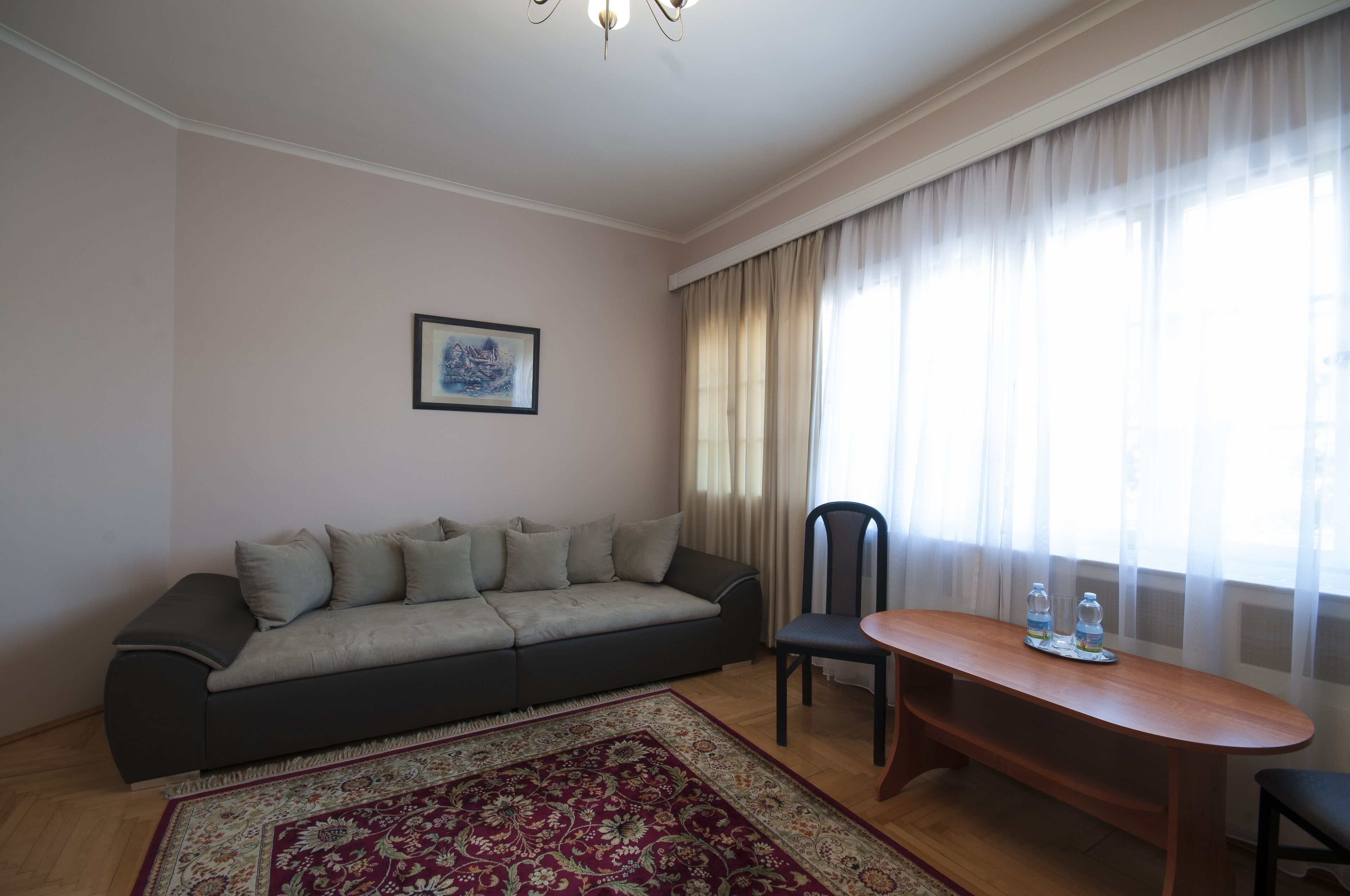 Uma sala de estar com sofá, mesa de jantar, uma cadeira, tapete e janela com cortinas.