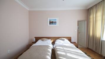 Quarto duplo com duas camas, cabeceira de madeira, um quadro emoldurado na parede e uma porta à direita.