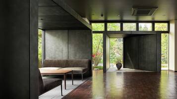 Um interior moderno com um sofá em tons escuros, uma mesa de madeira e uma janela grande com vista para o verde.