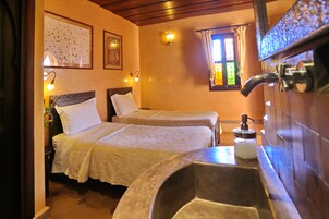 Quarto de hotel com duas camas, pia e janela com cortinas.