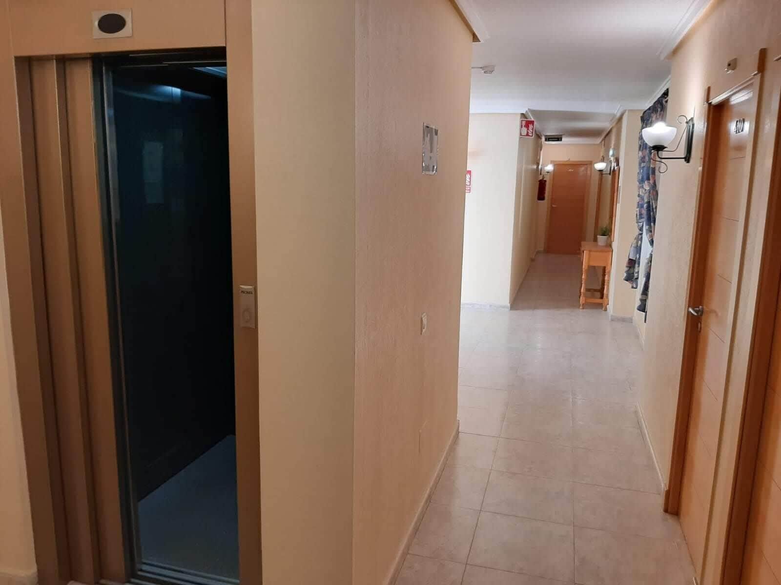Um corredor de hotel com uma porta de vidro à esquerda, um extintor de incêndio na parede e um suporte para casacos à direita.