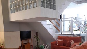 Uma sala de estar ampla com teto alto, uma escada, uma televisão, uma cadeira de balanço e um sofá vermelho.