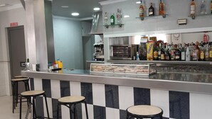 Uma área de bar com piso xadrez, banquetas e prateleiras com garrafas de bebidas.