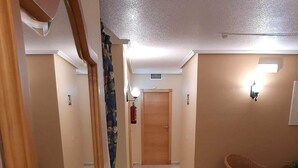 Um corredor com piso de madeira, uma porta de madeira no final e um vaso de planta em primeiro plano.