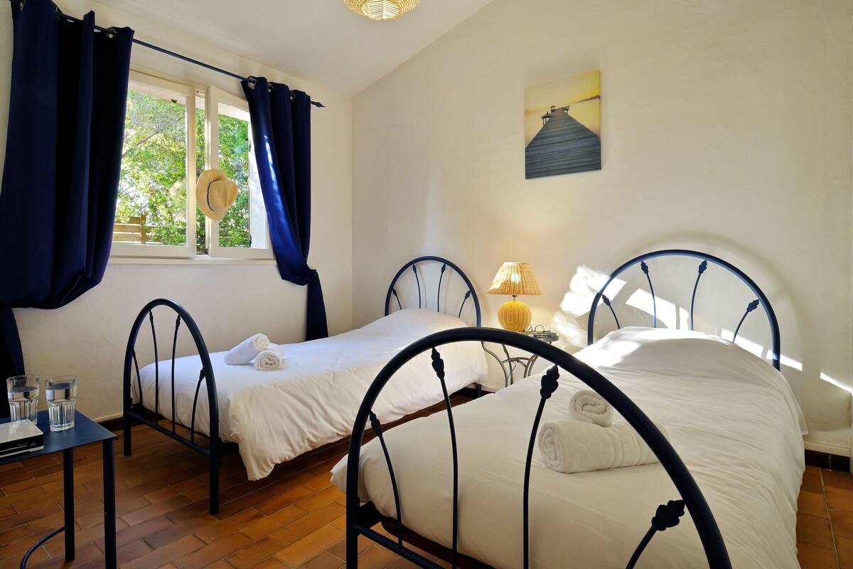 Quarto com duas camas, janela com cortinas, luminária e um quadro na parede.