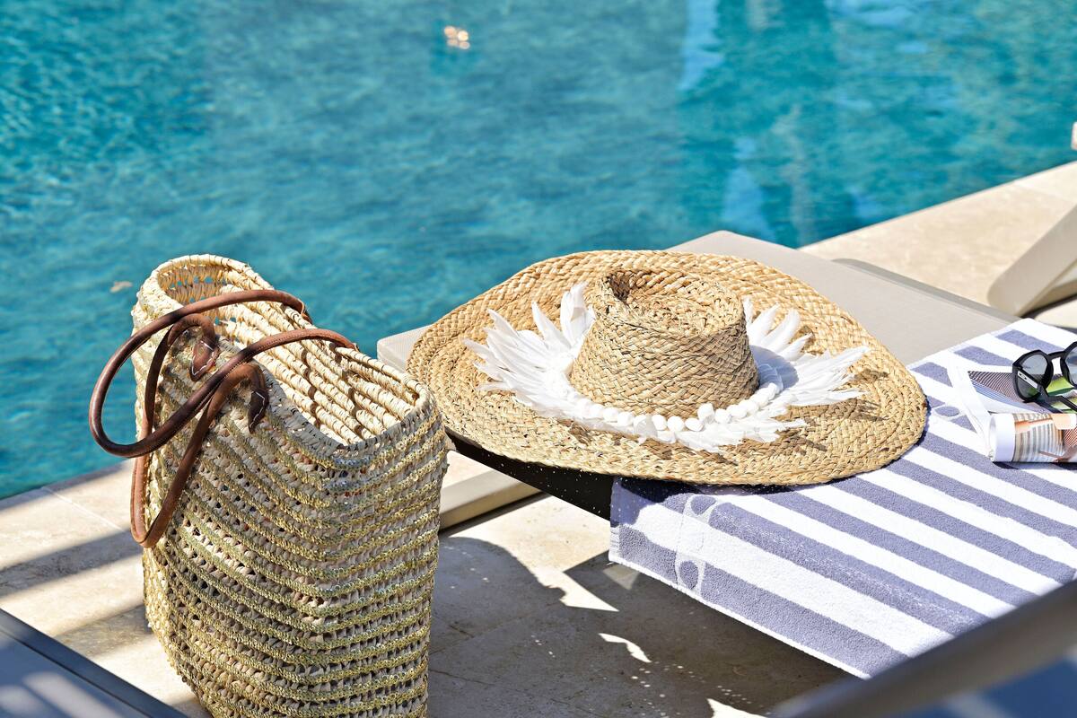 Uma bolsa de vime e um chapéu de palha numa espreguiçadeira à beira da piscina.