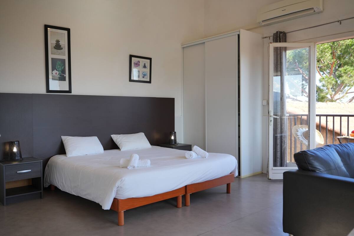 Quarto moderno com cama grande, mesa de cabeceira, cômoda e porta de vidro corrediça para uma varanda.