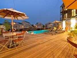 Um deck de madeira com piscina, cadeiras de sol e guarda-sóis.