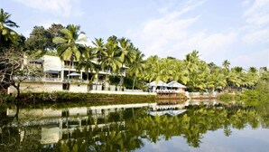 Um hotel tranquilo à beira do lago, com vários edifícios, incluindo um prédio principal com varandas e uma ala menor.
